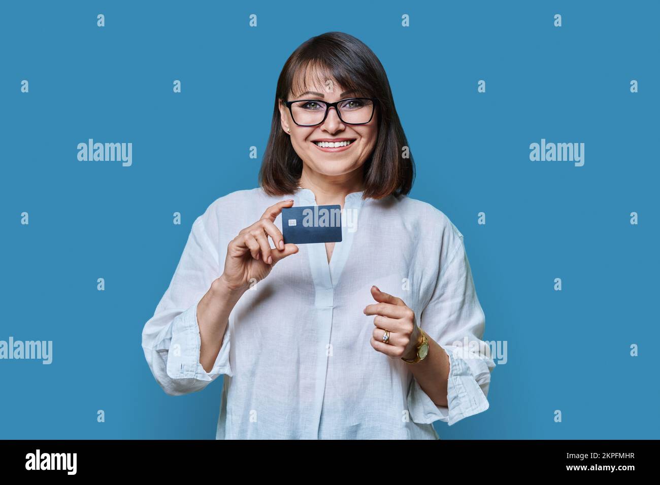 Attractive middle aged smiling woman holding plastic credit card, blue ...
