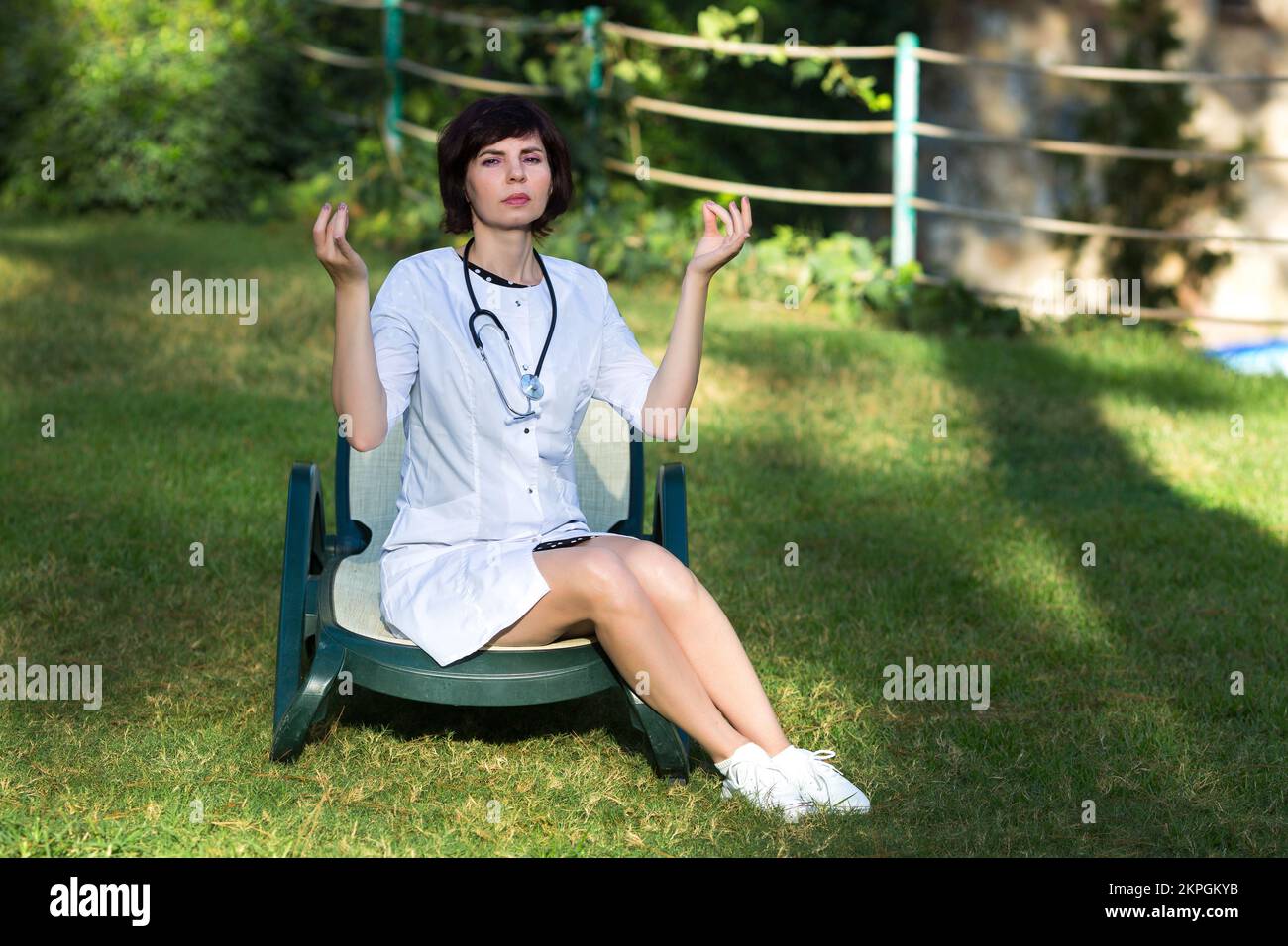 A female doctor is resting after a hard shift, doing yoga on the lawn ...