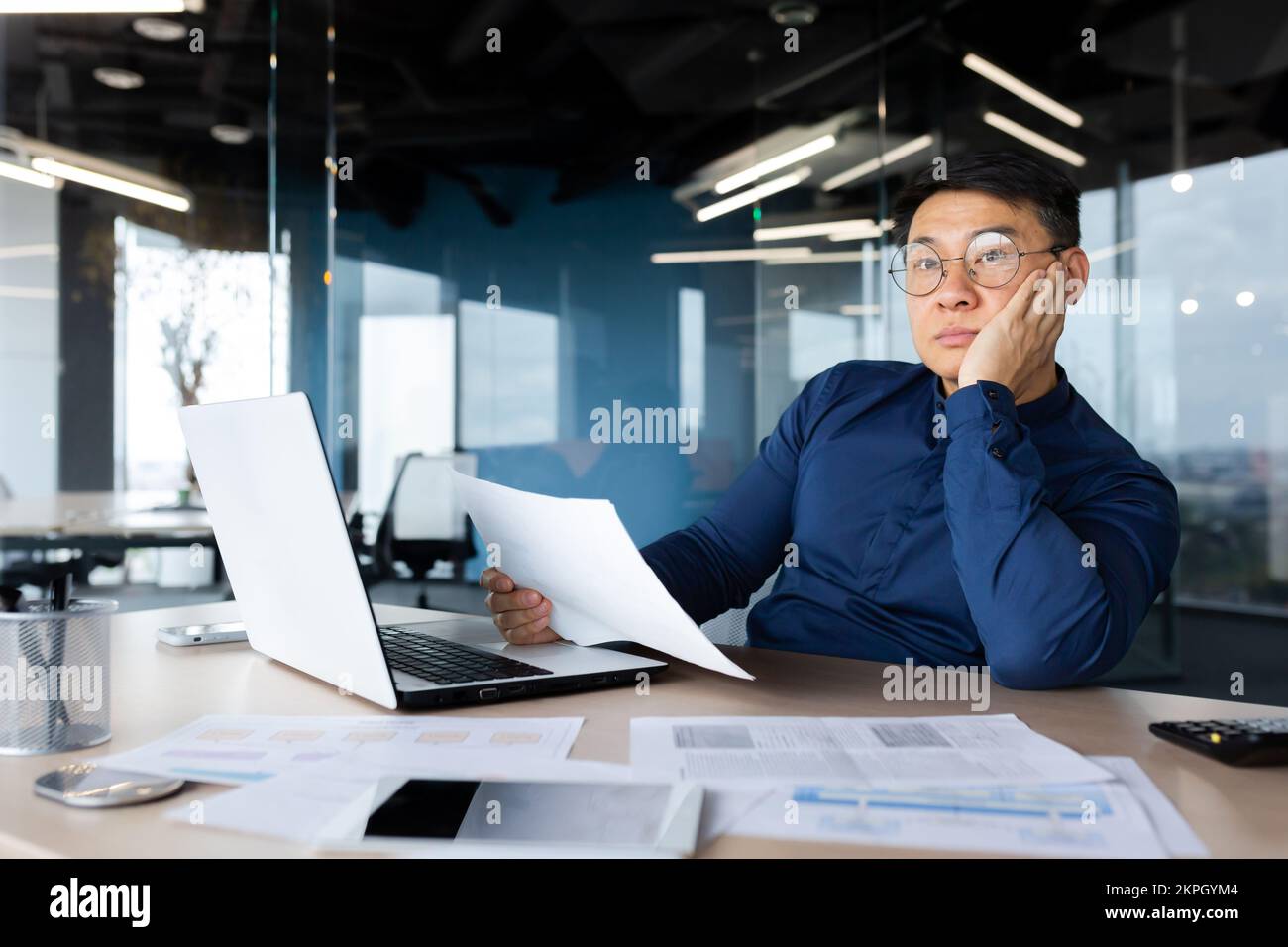 Serious thinking asian man working with documents inside office ...