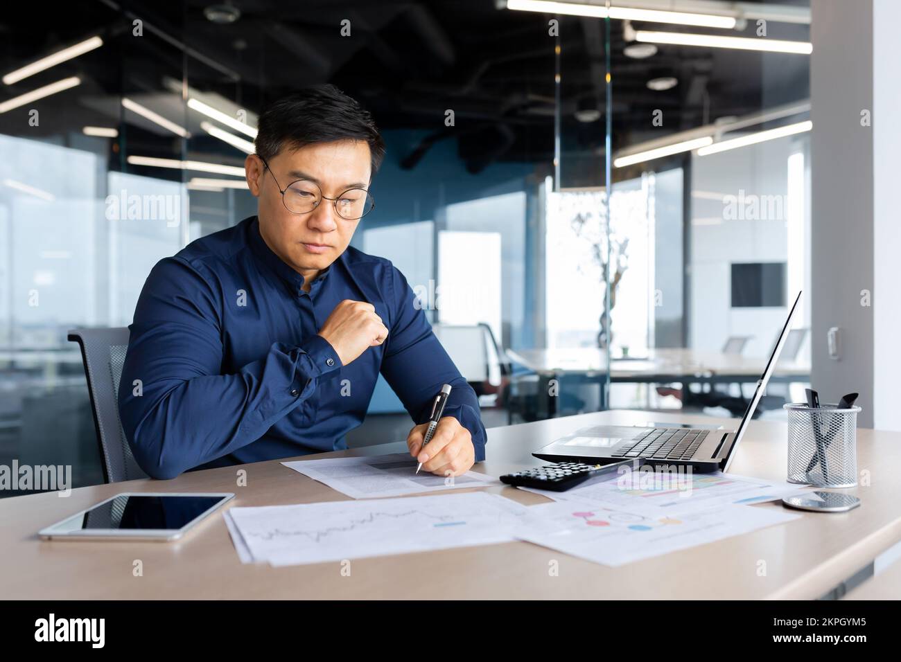 Serious thinking asian man working with documents inside office ...