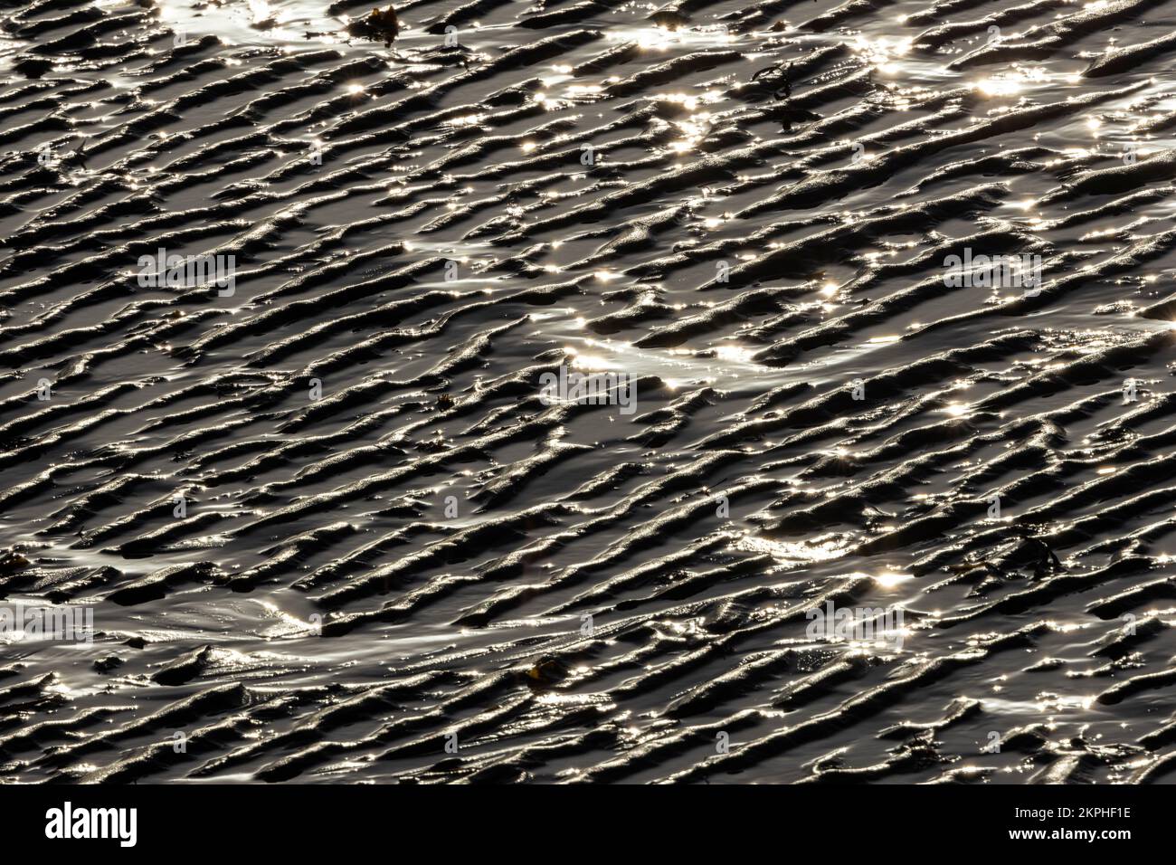 As the tide has receded on a sandy beach it leaves behind an abstract ...