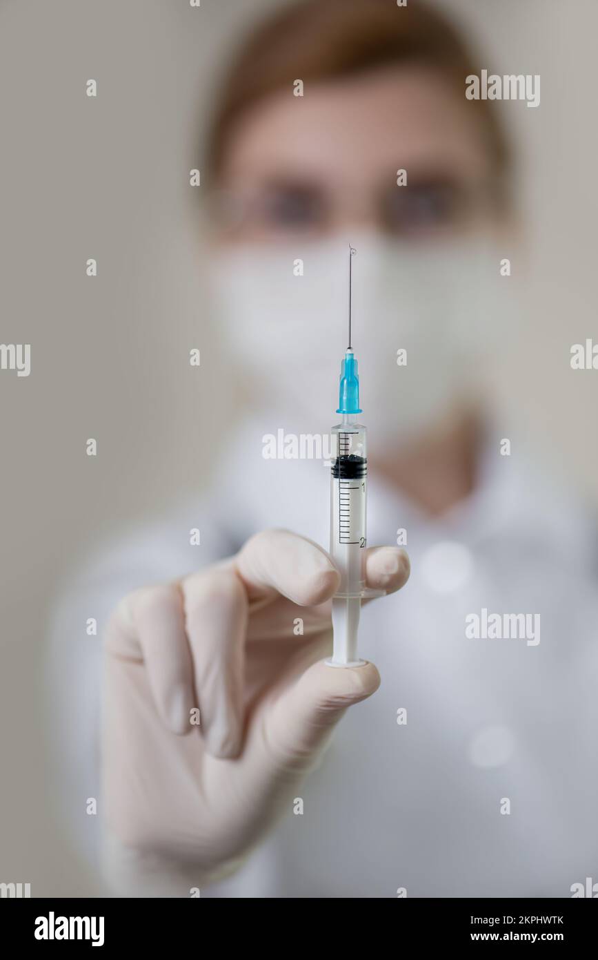 Woman in a medical uniform and mask with an injection syringe in hand ...
