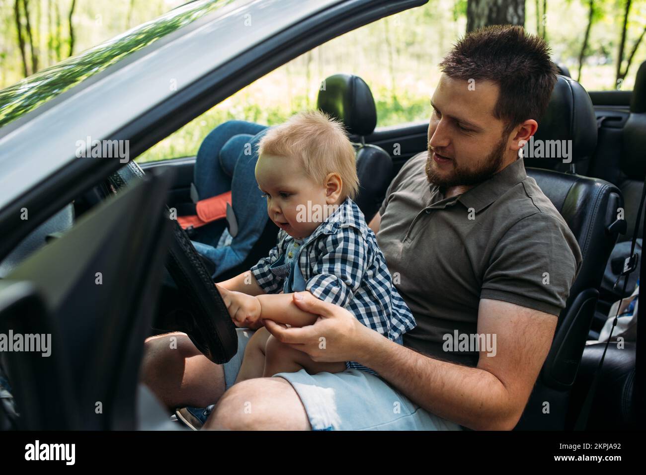 Dad shows his little son how to drive car while sitting behind wheel ...
