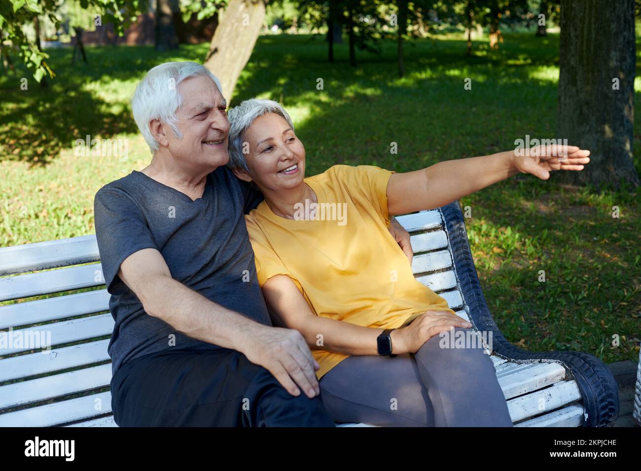 Pretty multi racial elderly 60s couple resting sit on bench in park ...