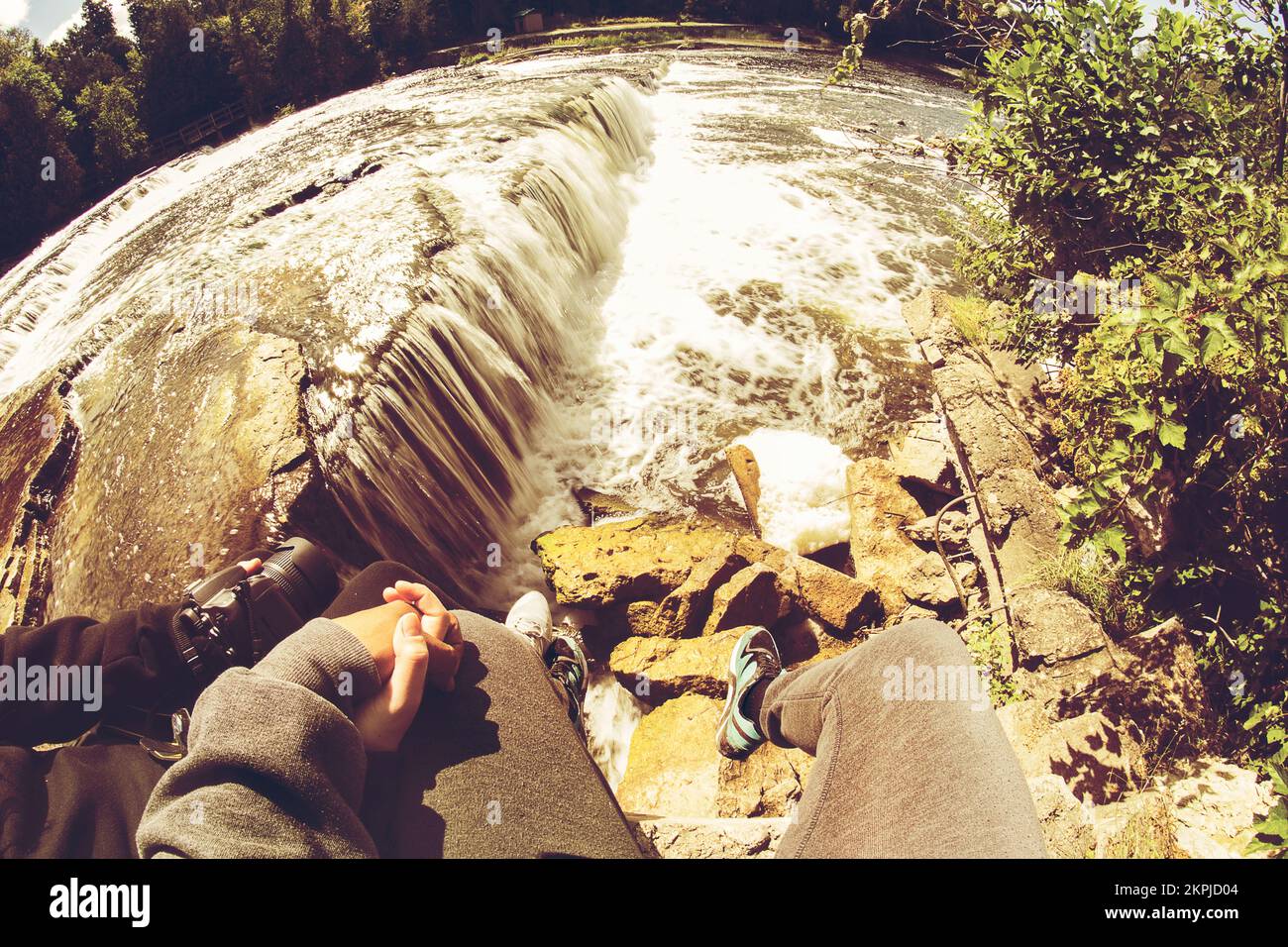 A couple holding hands sitting on the edge of a waterfall Stock Photo ...
