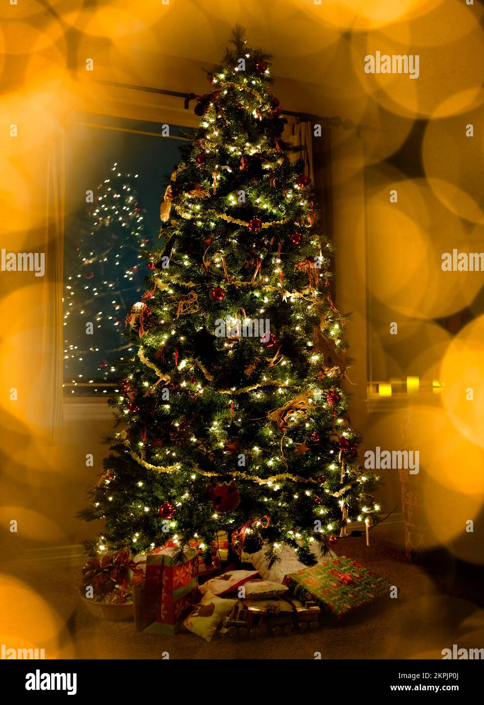 Christmas tree with lights and presents inside a home with big windows ...