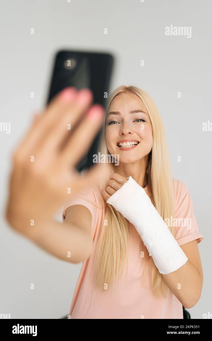 Vertical portrait of positive young blonde woman with broken arm ...