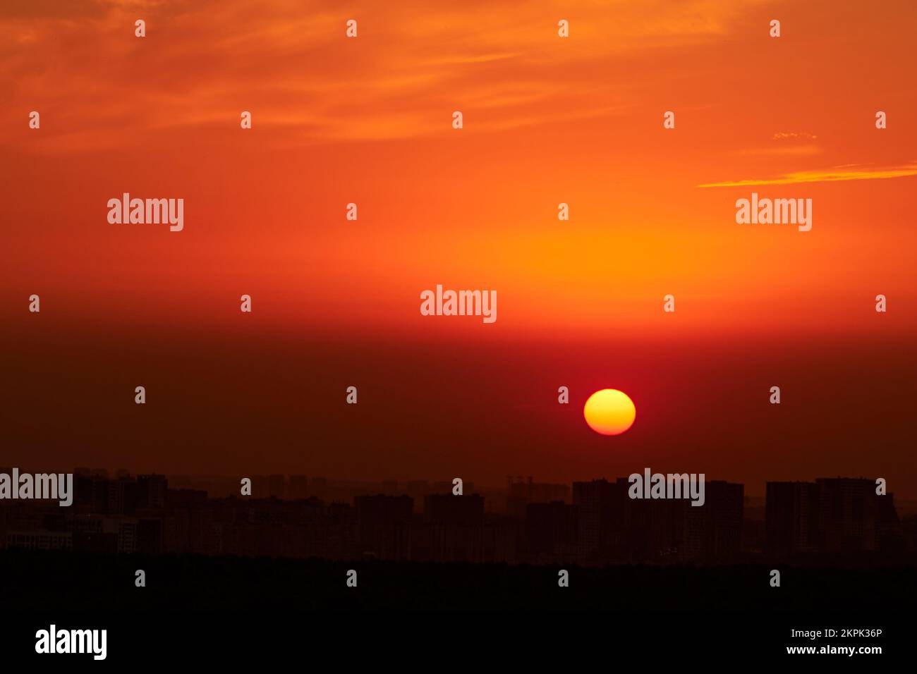 A big red sun in the sunset sky over the roofs of buildings, urban ...