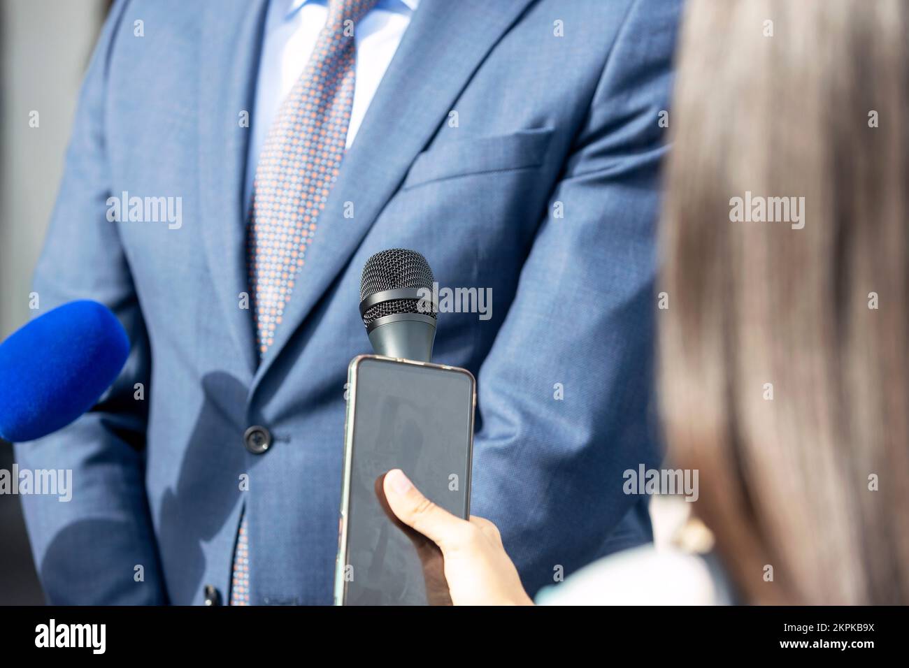 Journalist at news conference holding microphone and smartphone making ...
