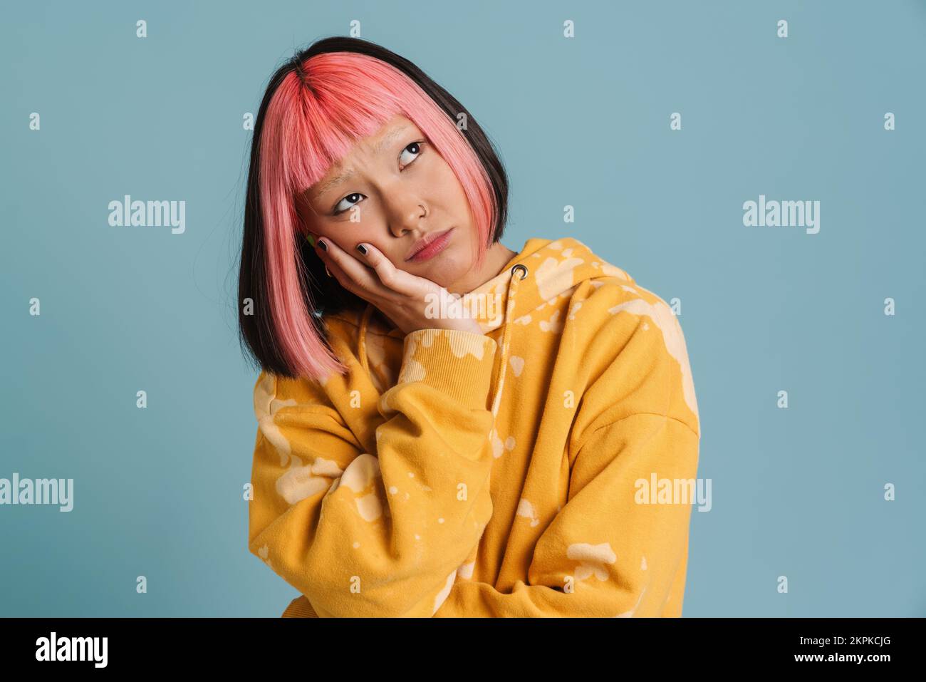Asian girl with pink hair and piercing frowning while looking aside ...