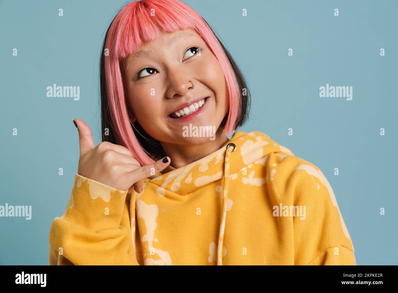 Asian girl with pink hair and piercing making handset gesture isolated ...