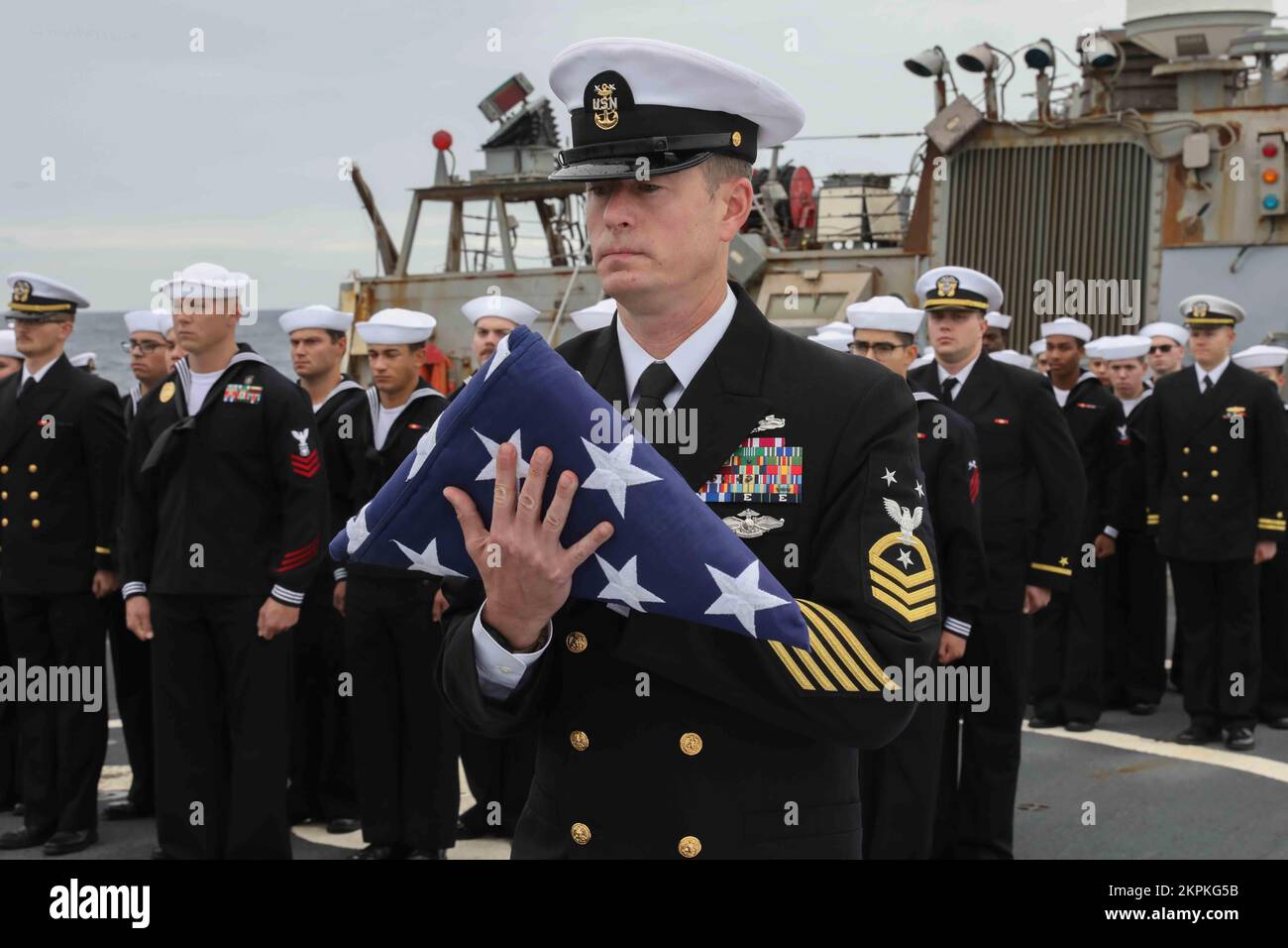 Command Master Chief Brandon Ellison holds the ensign during a burial ...