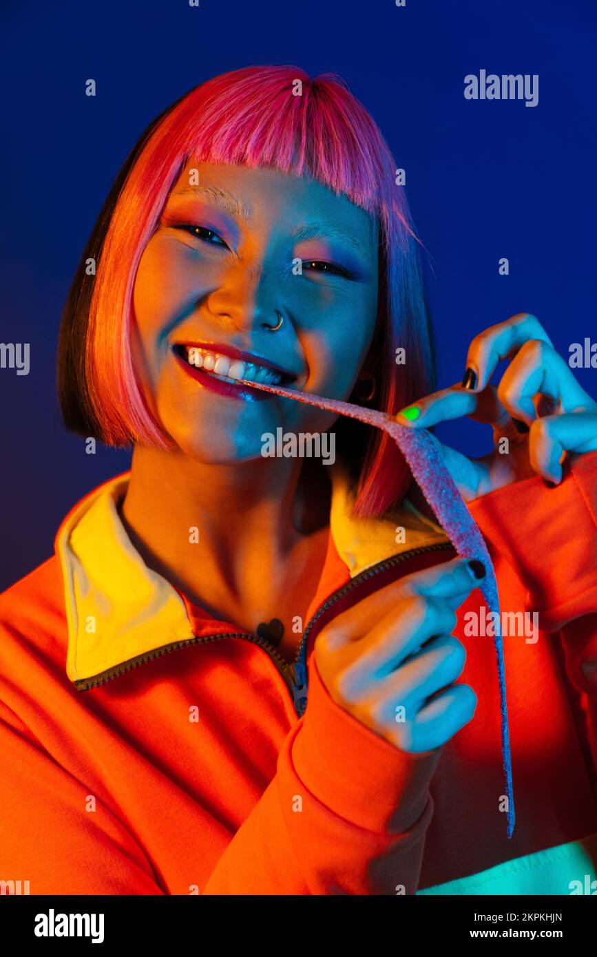 Asian girl with pink hair making fun while eating chewing marmalade ...