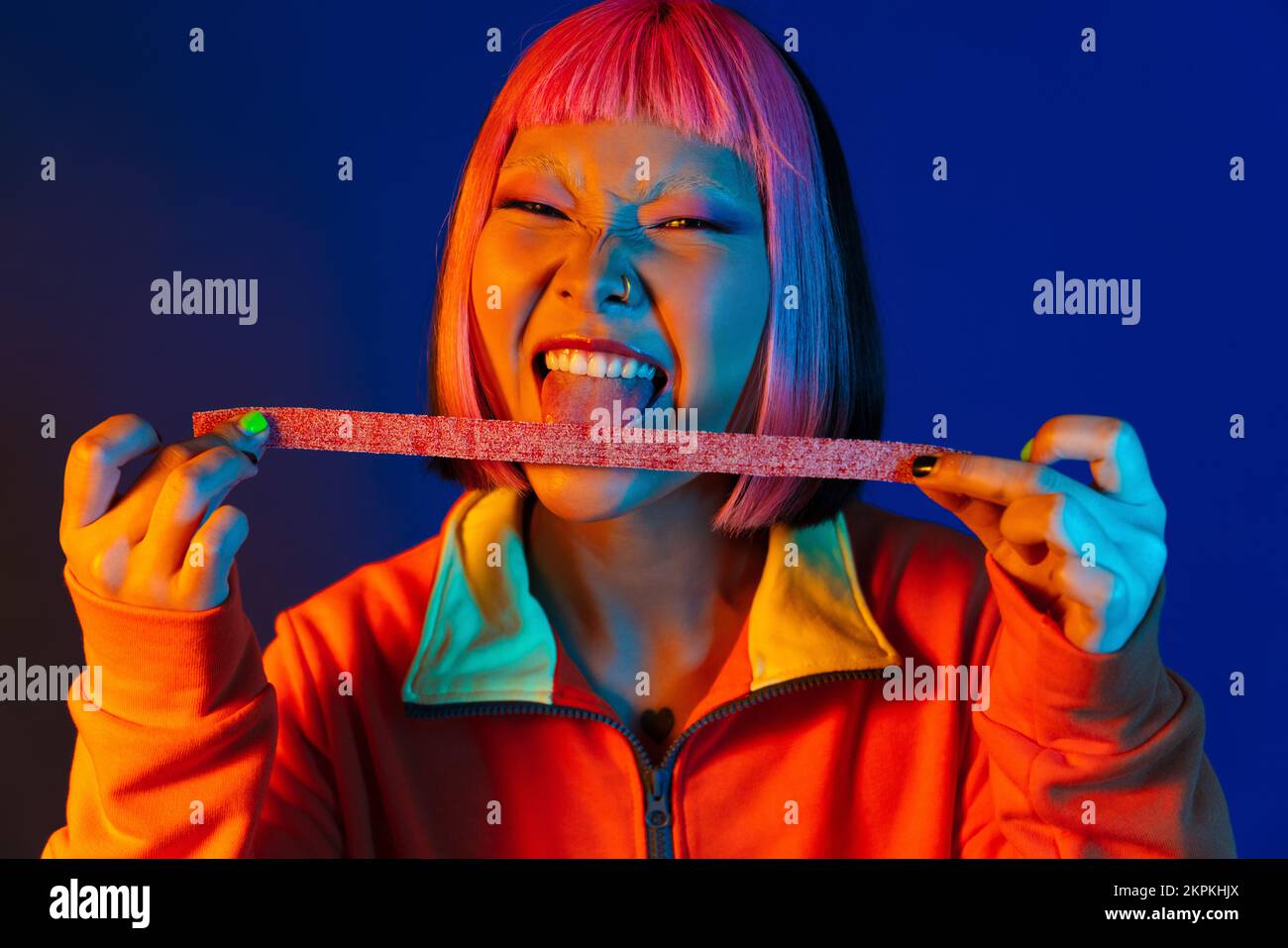 Asian girl with pink hair making fun while eating chewing marmalade ...