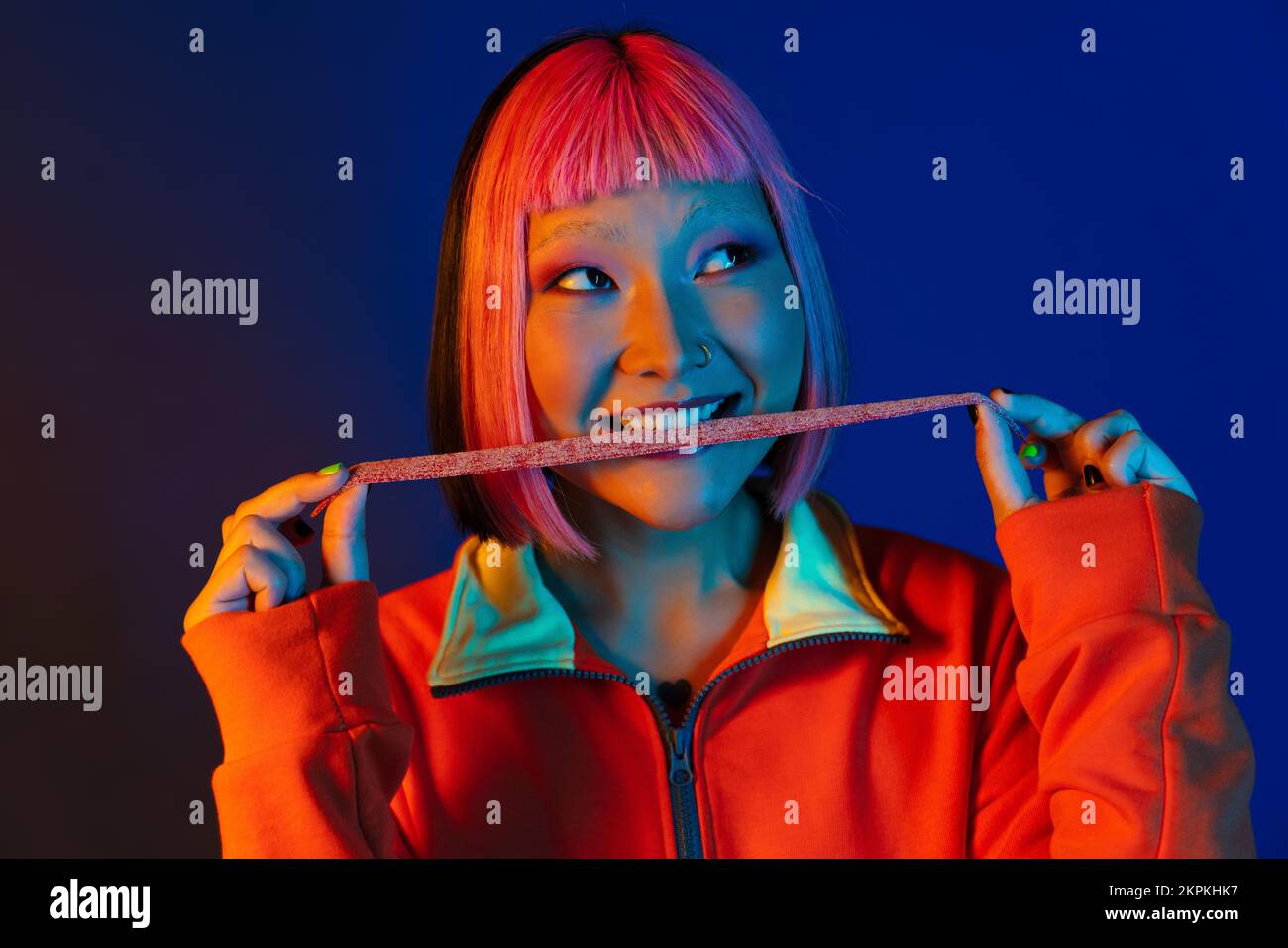 Asian girl with pink hair making fun while eating chewing marmalade ...