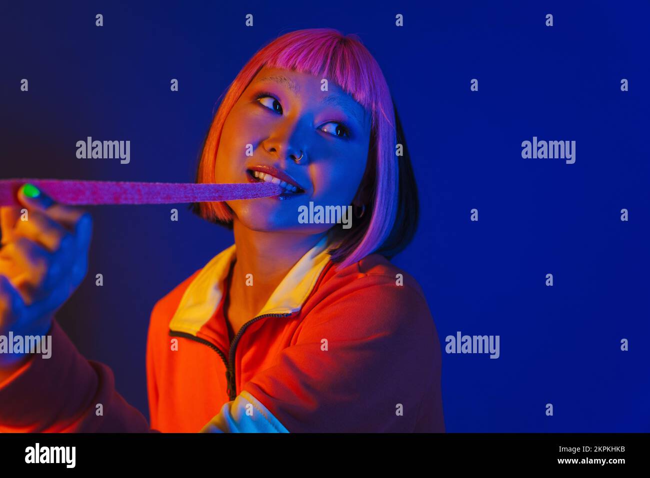 Asian girl with pink hair making fun while eating chewing marmalade ...