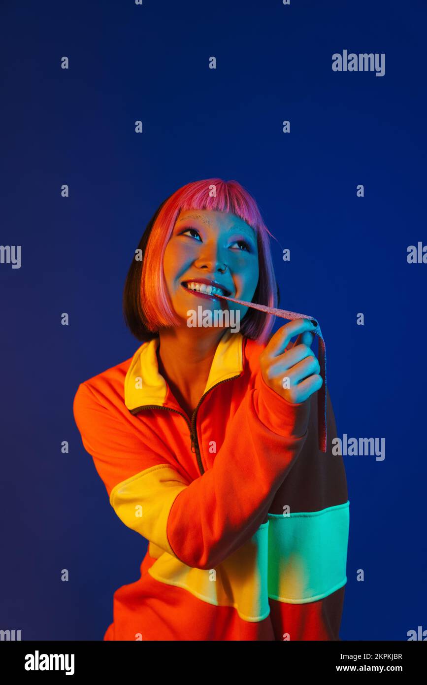 Asian girl with pink hair making fun while eating chewing marmalade ...