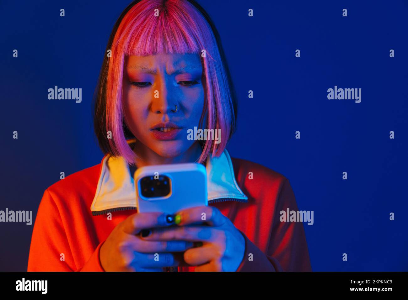 Asian girl with piercing frowning and using mobile phone isolated over ...