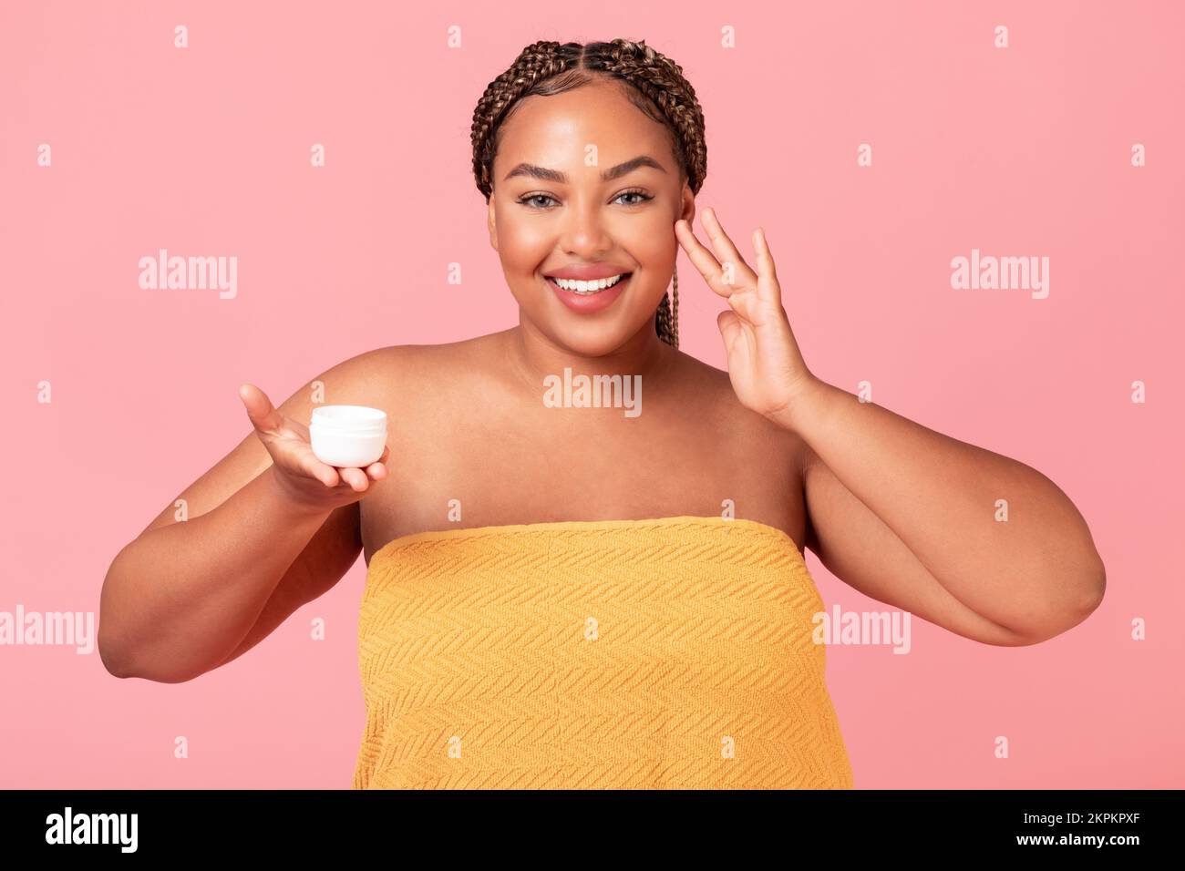 Happy black obese woman applying moisturising cream on face, standing ...