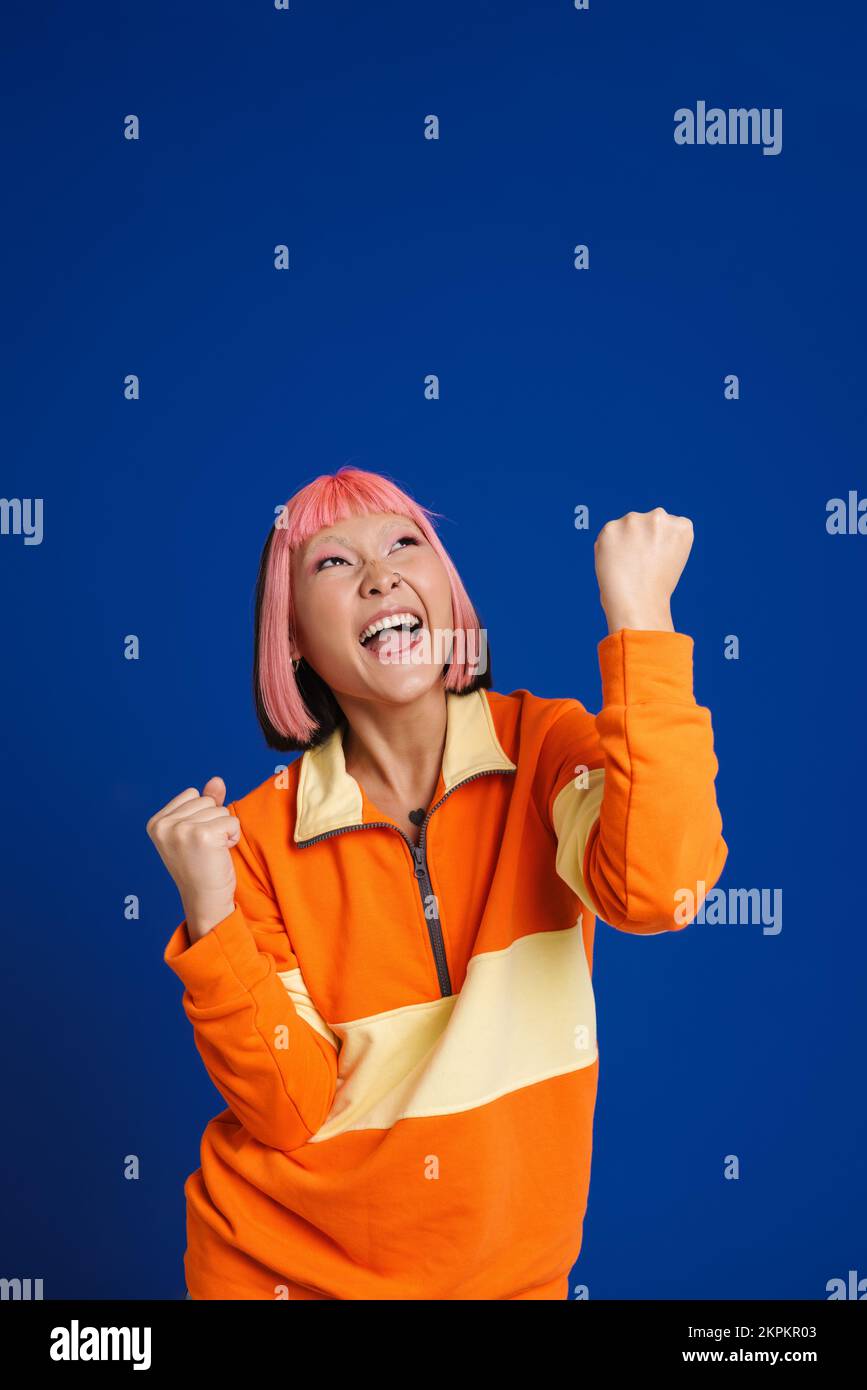 Asian girl with pink hair screaming while making winner gesture ...