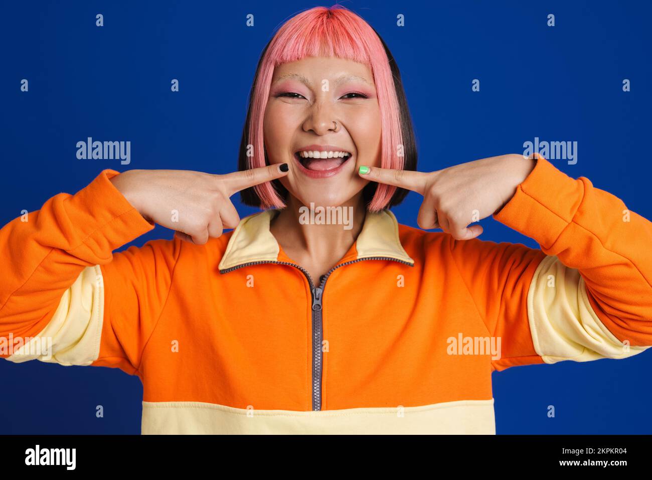 Asian girl with pink hair and piercing pointing fingers at her smile ...