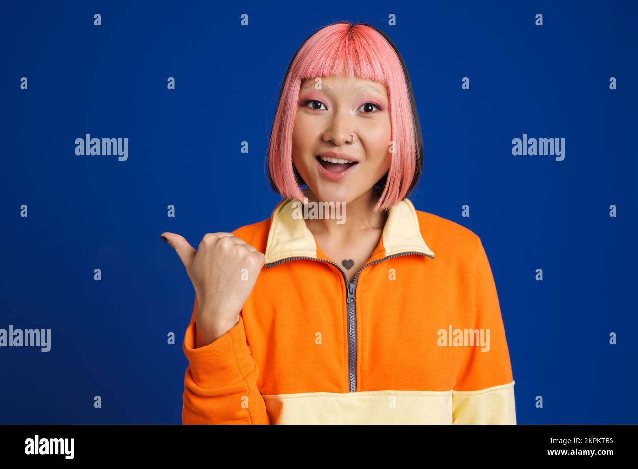 Asian surprised girl with pink hair pointing finger aside isolated over ...