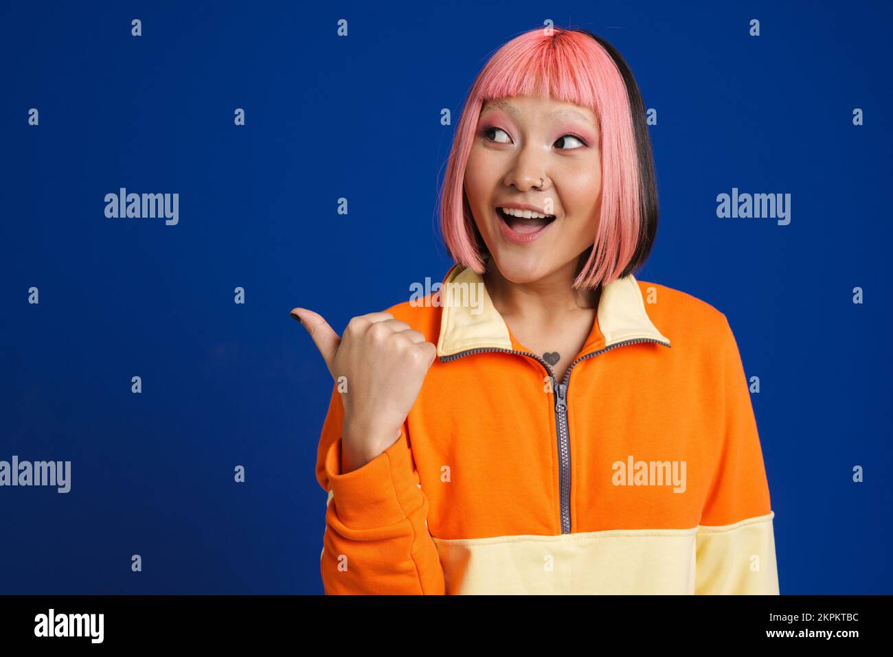 Asian surprised girl with pink hair pointing finger aside isolated over ...