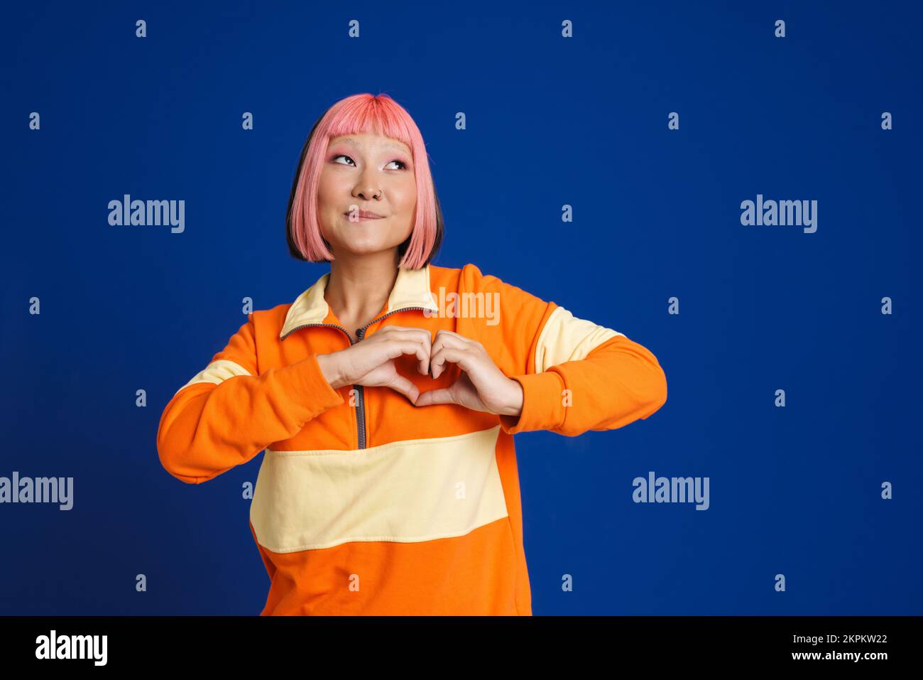 Asian girl with pink hair laughing and showing heart gesture isolated ...