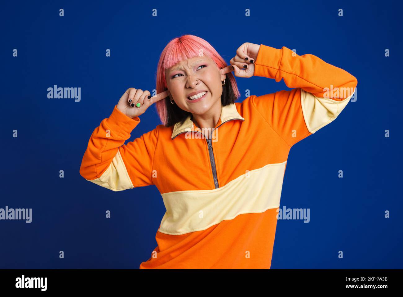 Asian girl with pink hair frowning and plugging her ears isolated over ...