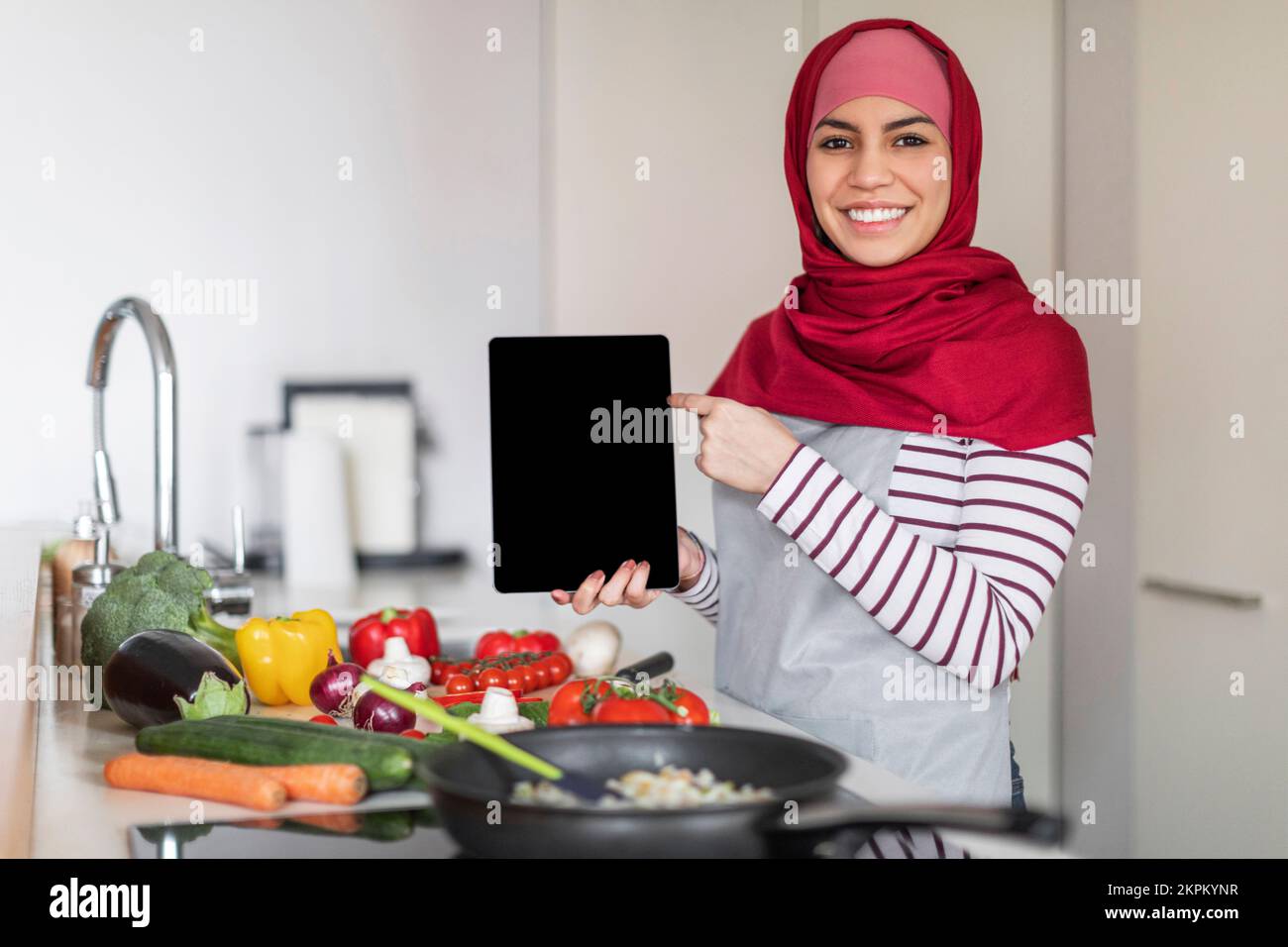 Pretty muslim woman cooking at home, showing digital tablet, mockup ...