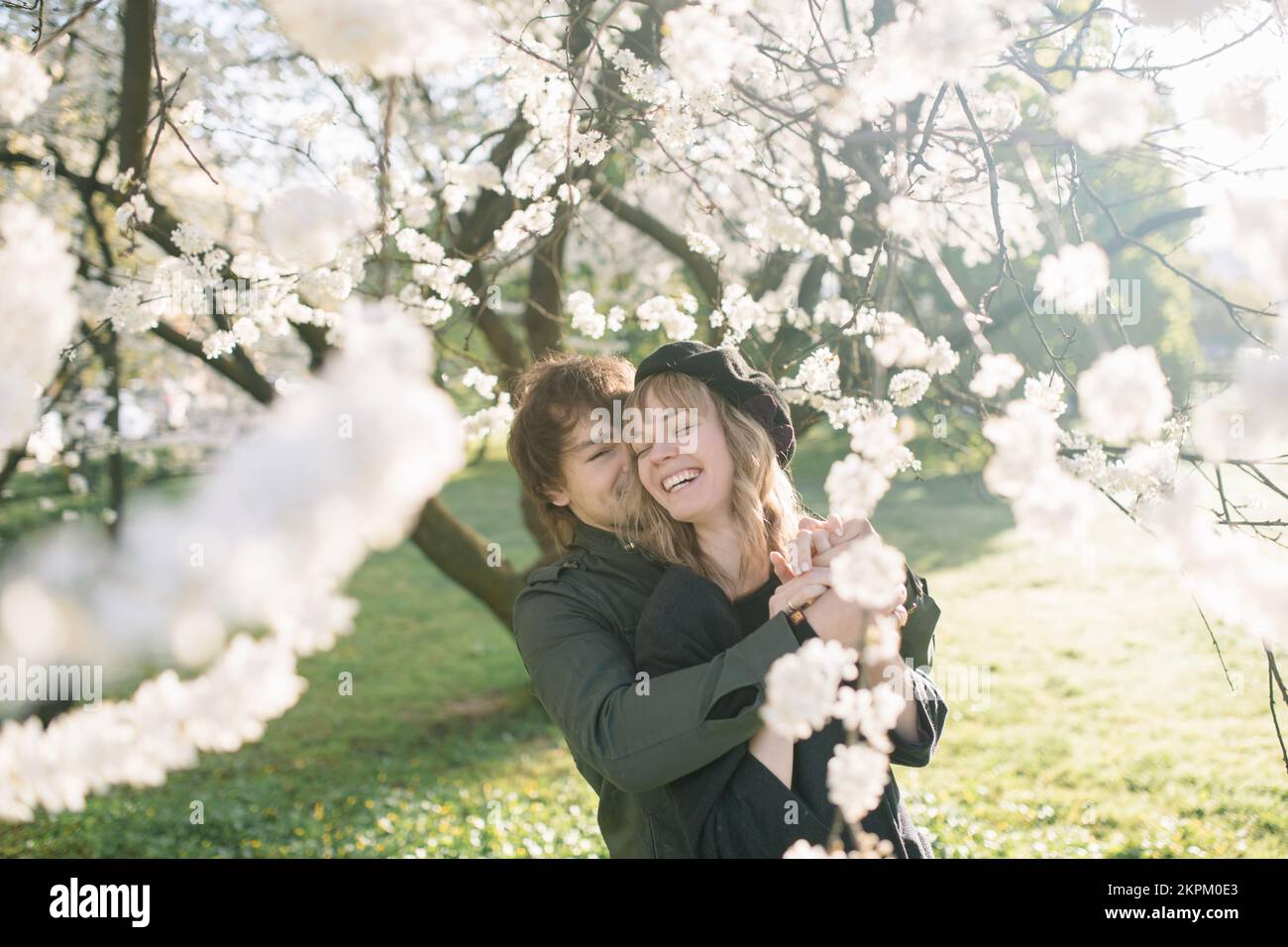 Smiling happy couple hugging each other under a cherry blossom tree in ...
