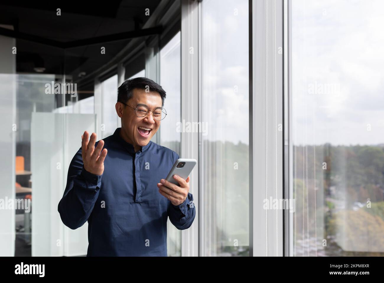 Asian man using phone standing near window inside office building ...