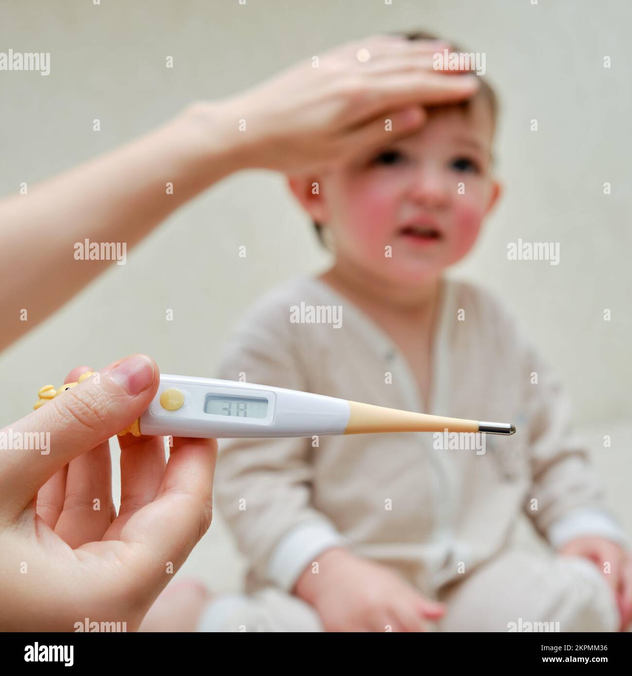 A mother woman measures the temperature of a sick toddler baby with a thermometer. Mom checks ...