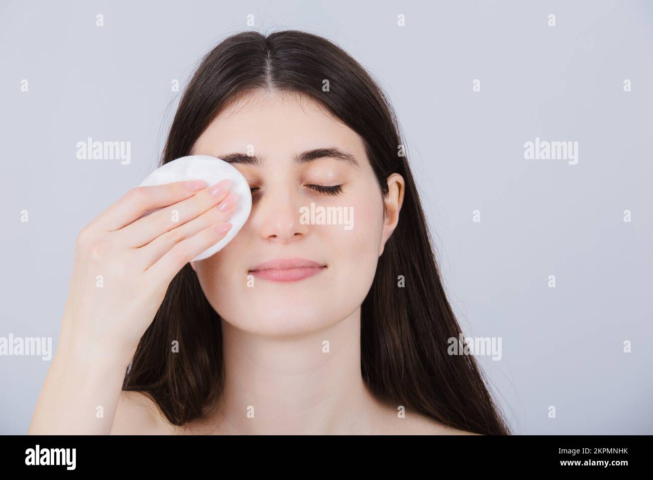 Young woman cleaning her face with cotton pad isolated on white ...