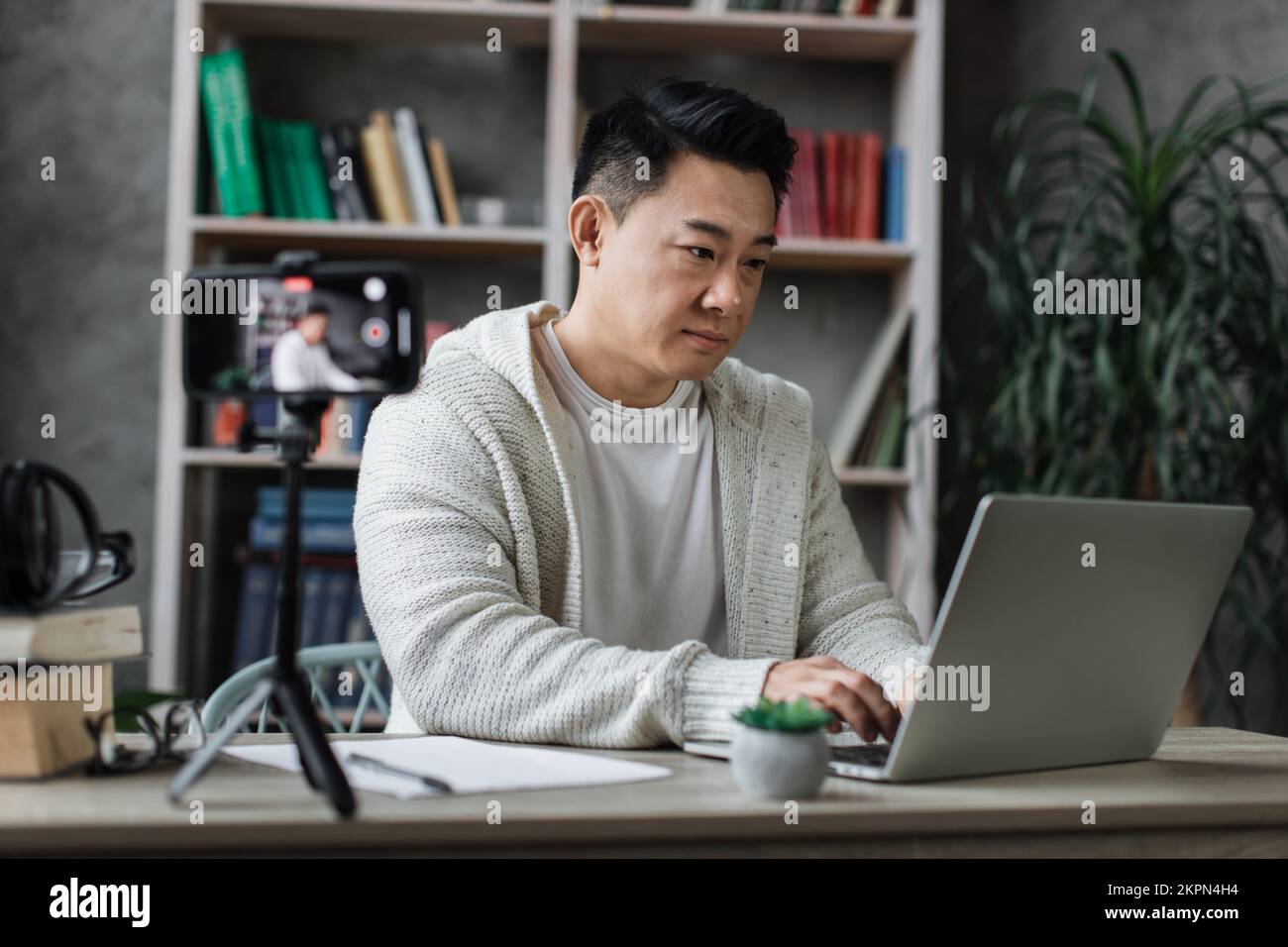 Pleasant young asian man working on laptop while recording video on his ...