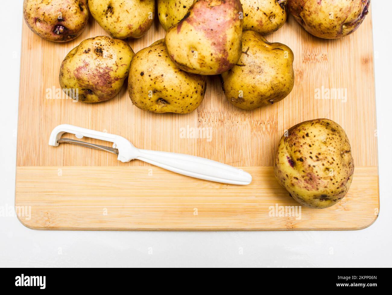 Food prep in progress with peeling knife on wood board with unpeeled ...