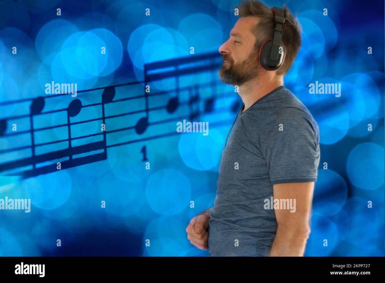 Young man over isolated blue wall with sheet music listening to music ...