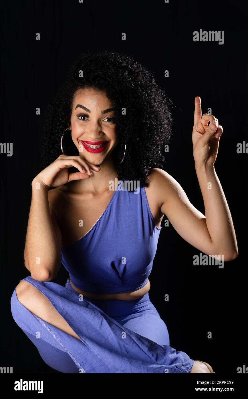 Portrait of young beautiful woman, sitting, pointing up, wearing blue ...