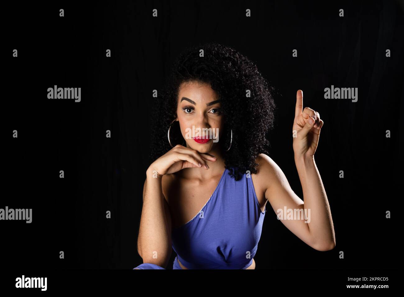 Portrait of young beautiful woman, sitting, pointing up, wearing blue ...