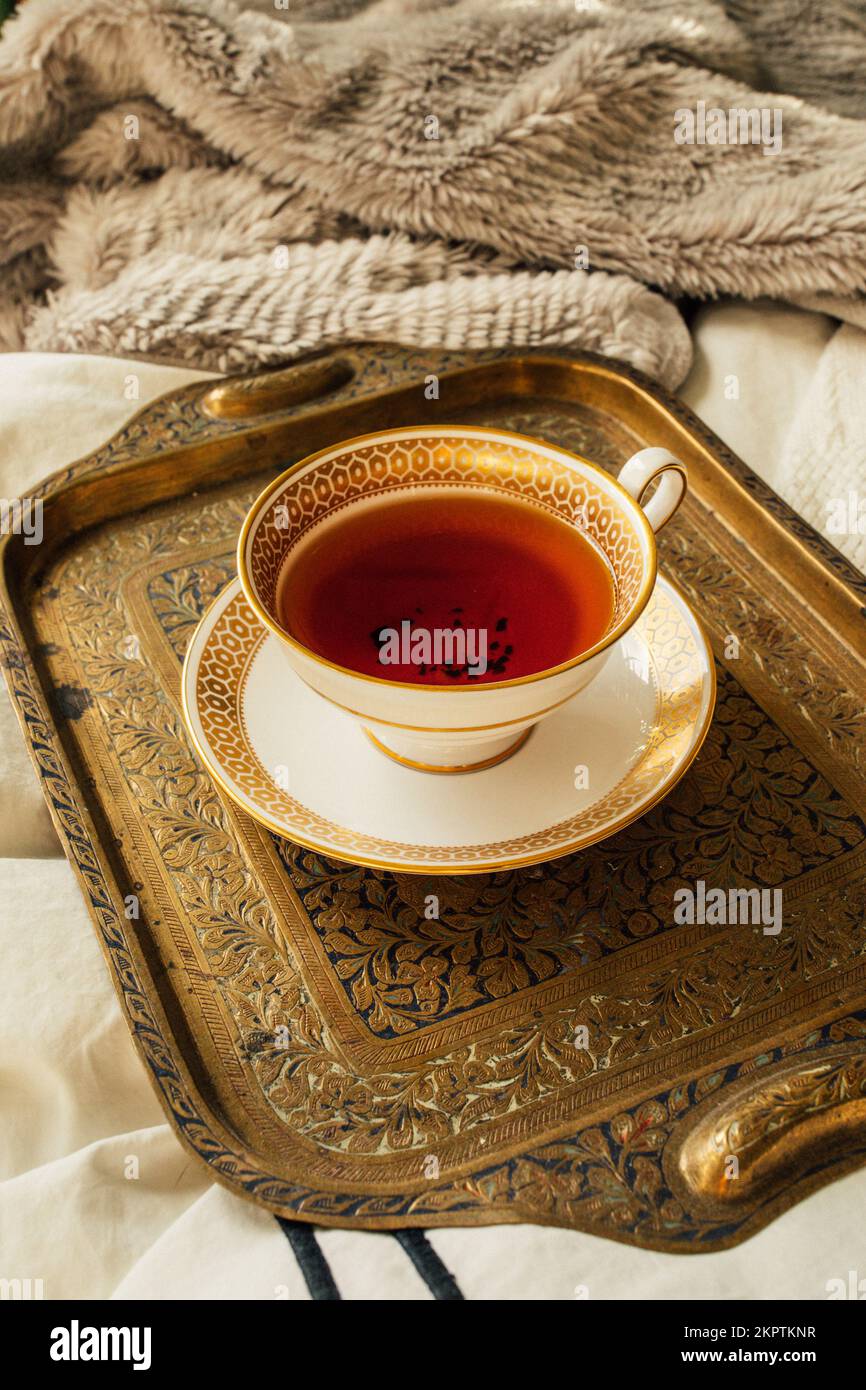 black tea in fancy gold and white teacup on brass tray on bed with ...