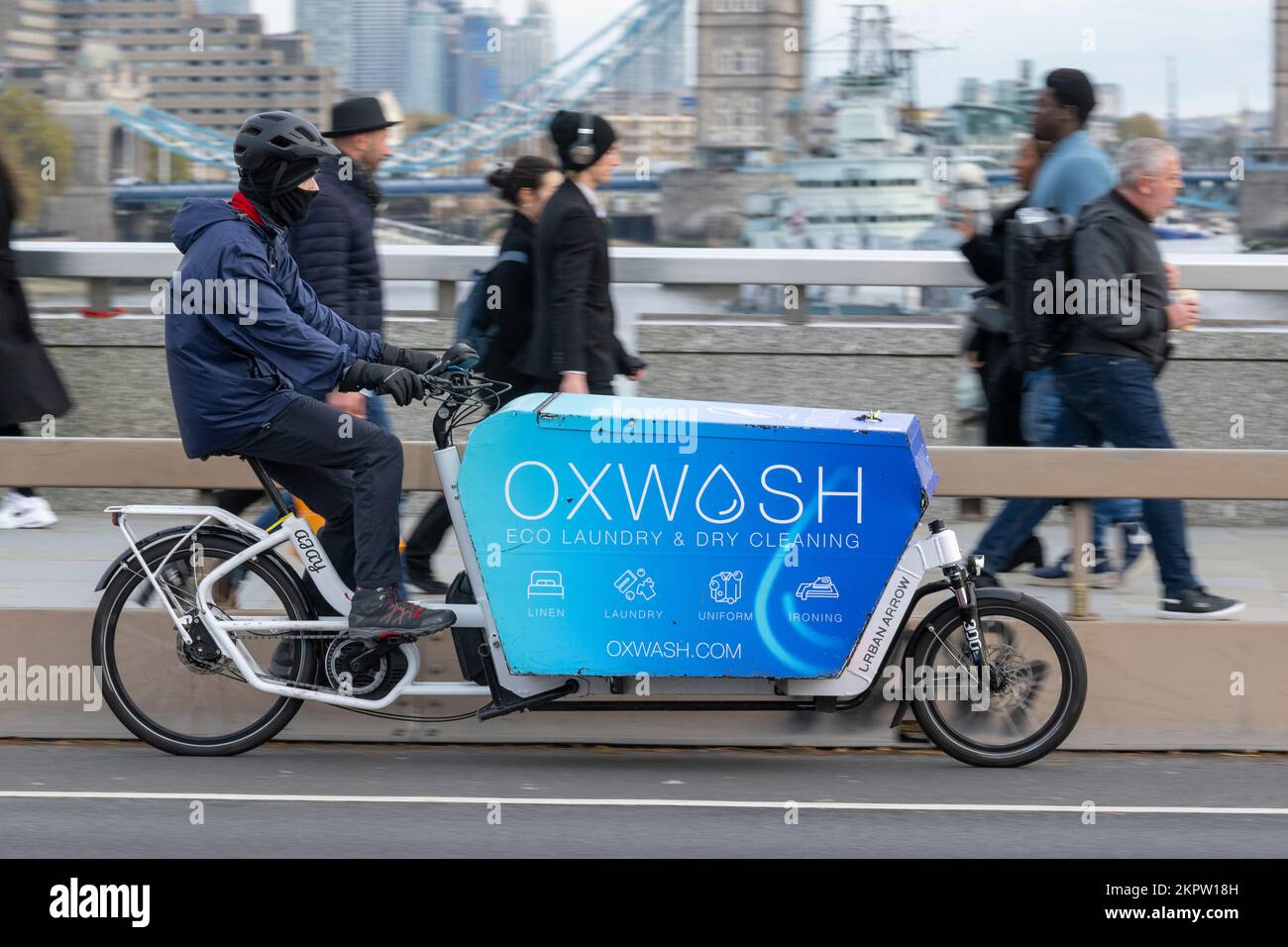 A Oxwash cycle courier riding an Urban Arrow e-cargo bike across, London Bridge, London, UK. 17 ...