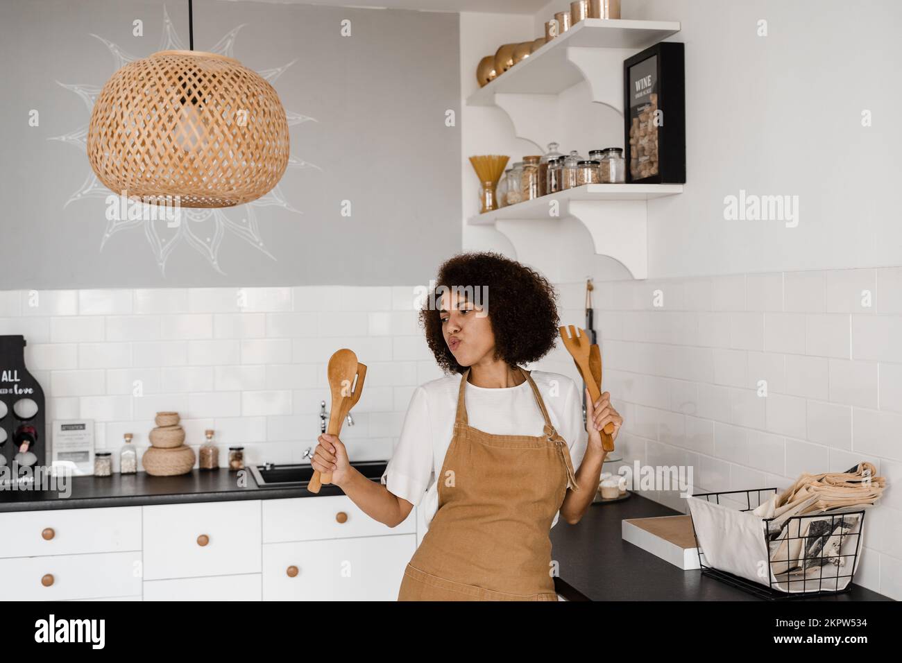 Happy african housewife in apron singing and dancing on the kitchen ...