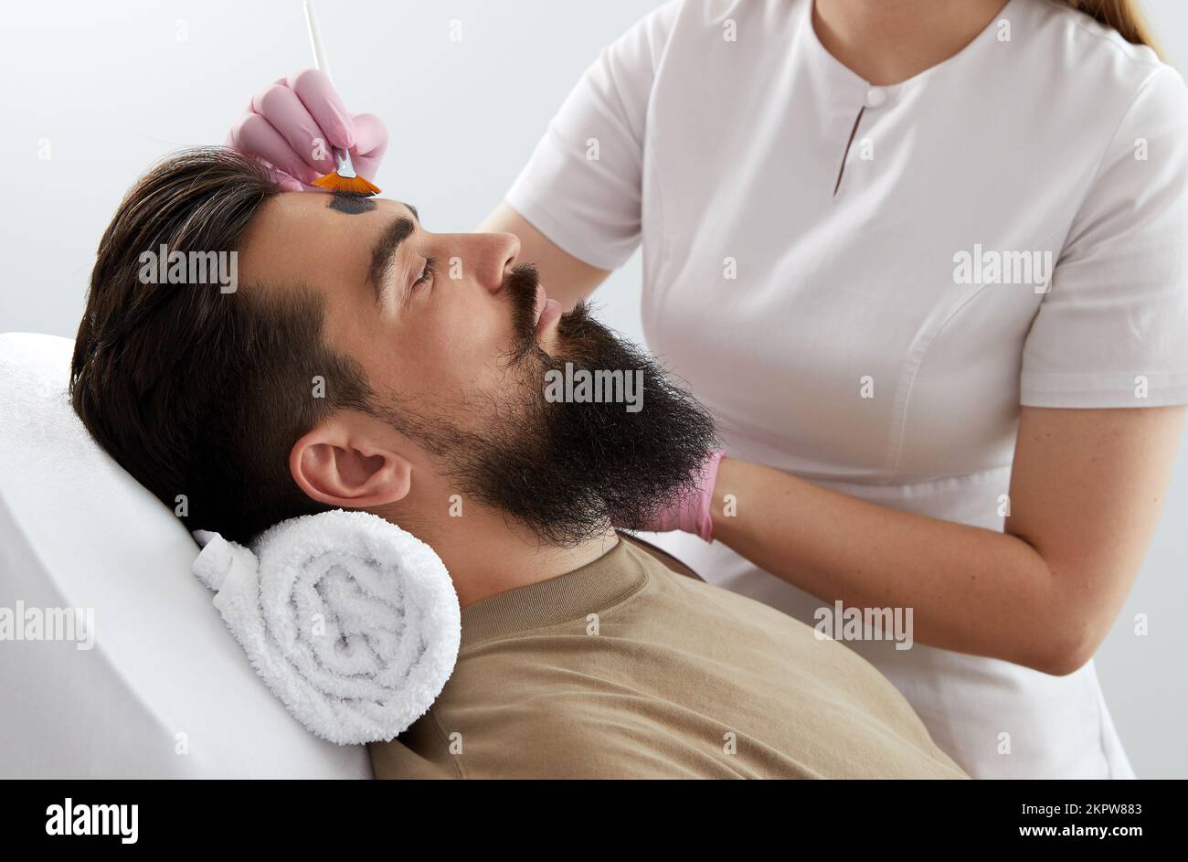Cosmetologist applying a clay mask to male face with brush. Spa ...