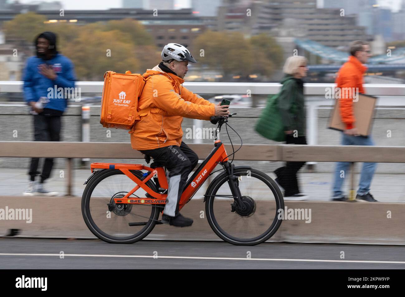 A Just Eat cycle courier riding an e-bike across, London Bridge, London ...