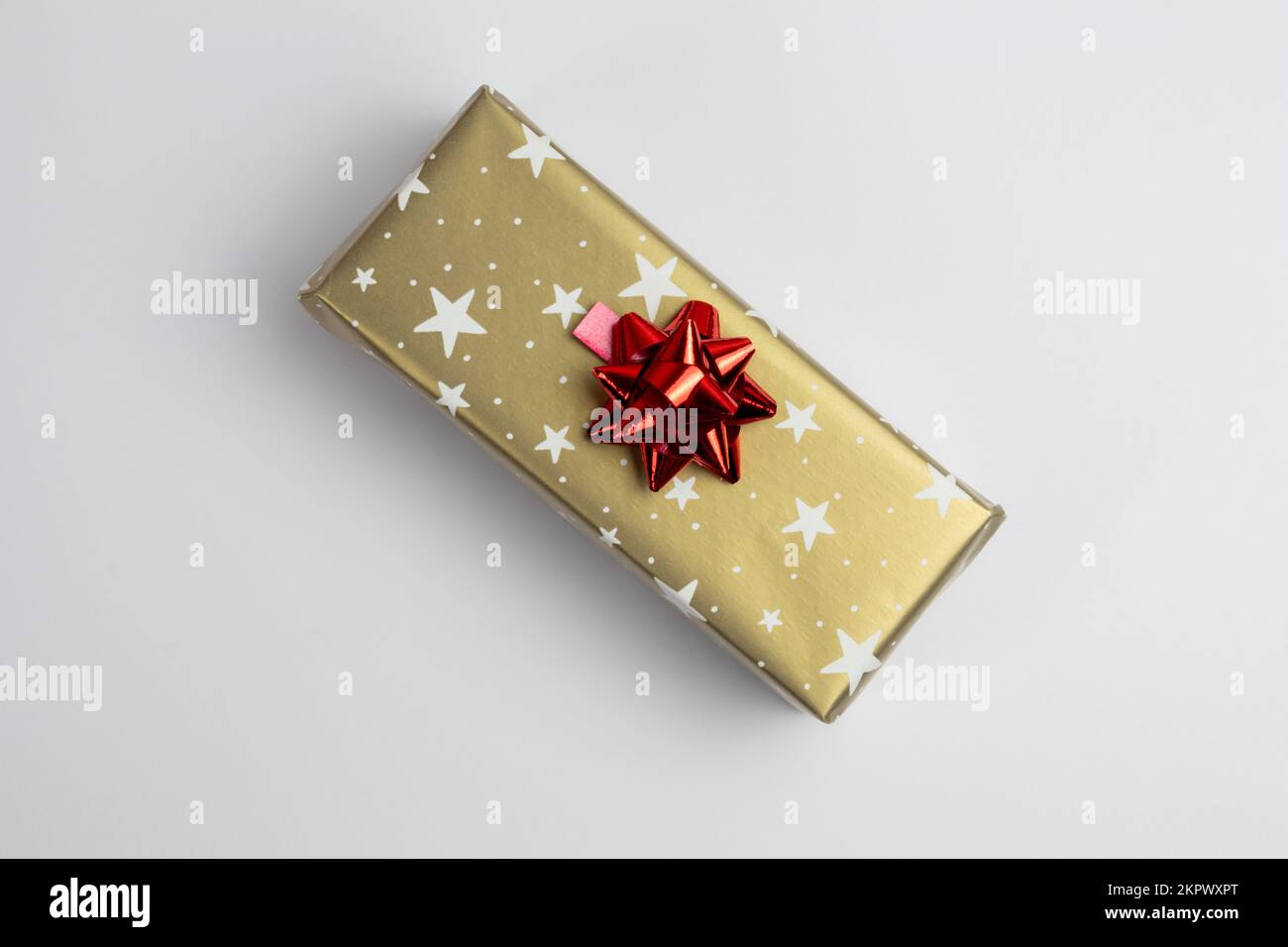 One wrapped present in golden paper with red bow top view on grey or ...