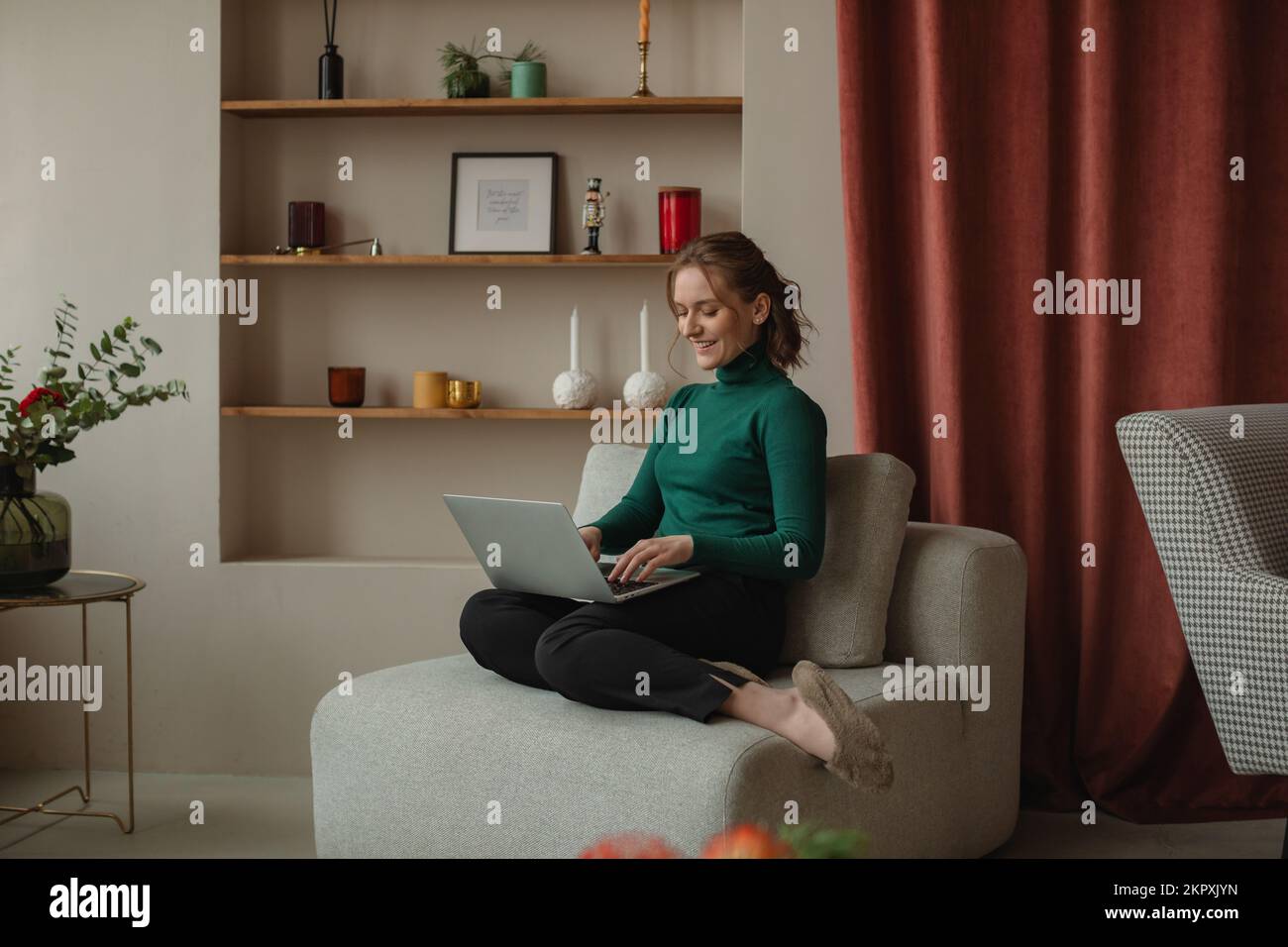 Smiling woman sitting on a chair in the living room using her laptop ...