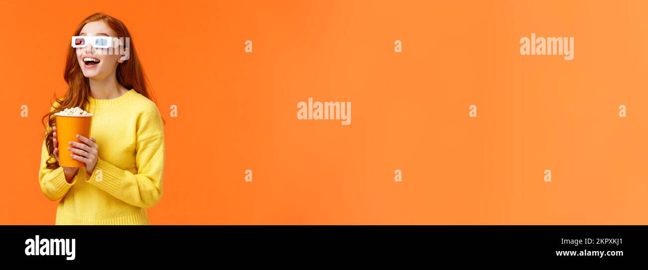 Girl eating popcorn, smiling amused as staring at large screen watching ...