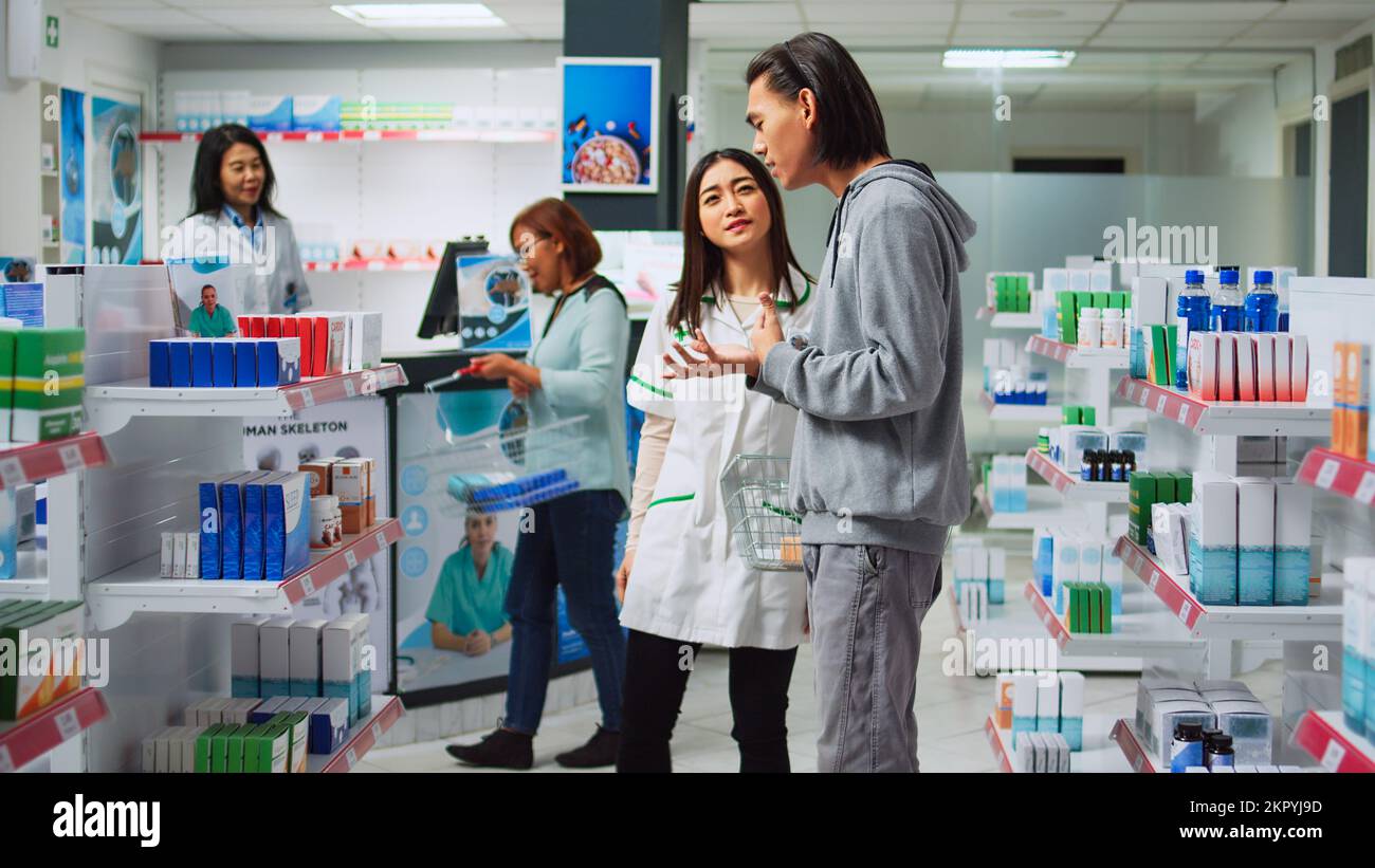 Asian worker explaining pharmacy leaflet in medical retail store ...