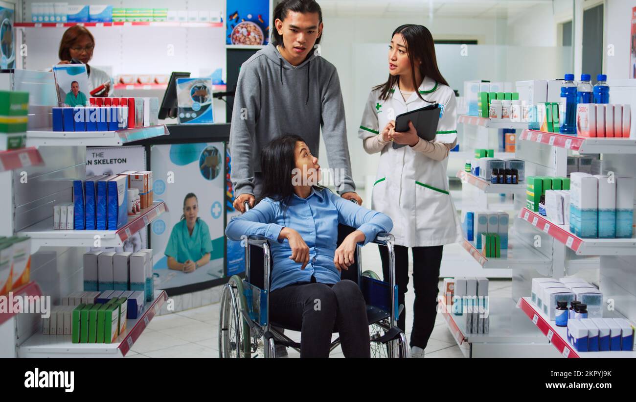 Pharmacy employee giving pills box to woman in wheelchair, male ...