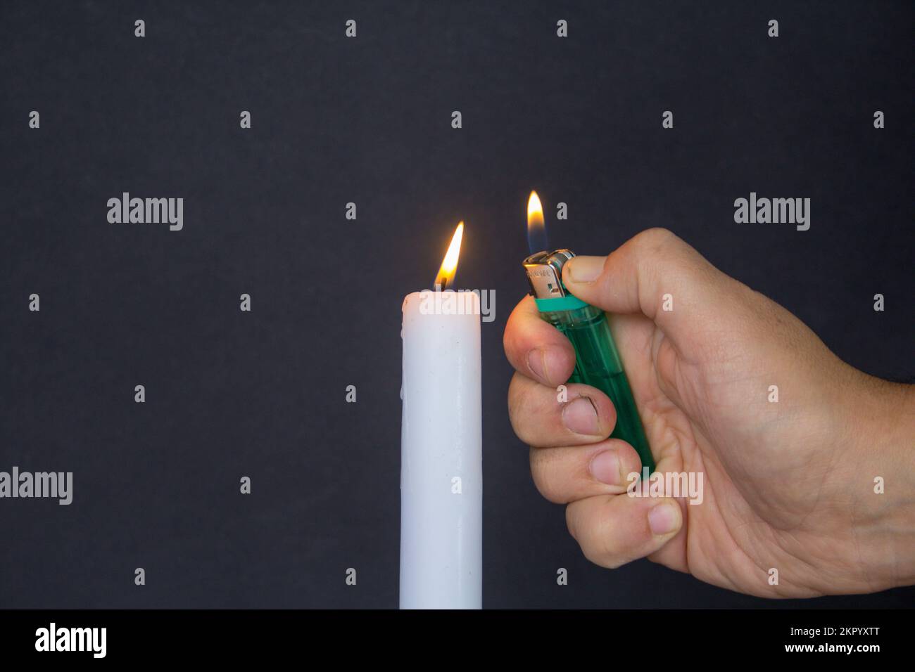 A man's hand holding a lighter while lighting a candle against a black ...